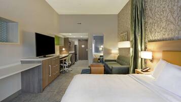 Quarto de hotel com cama, escrivaninha, televisão e vista para o corredor.