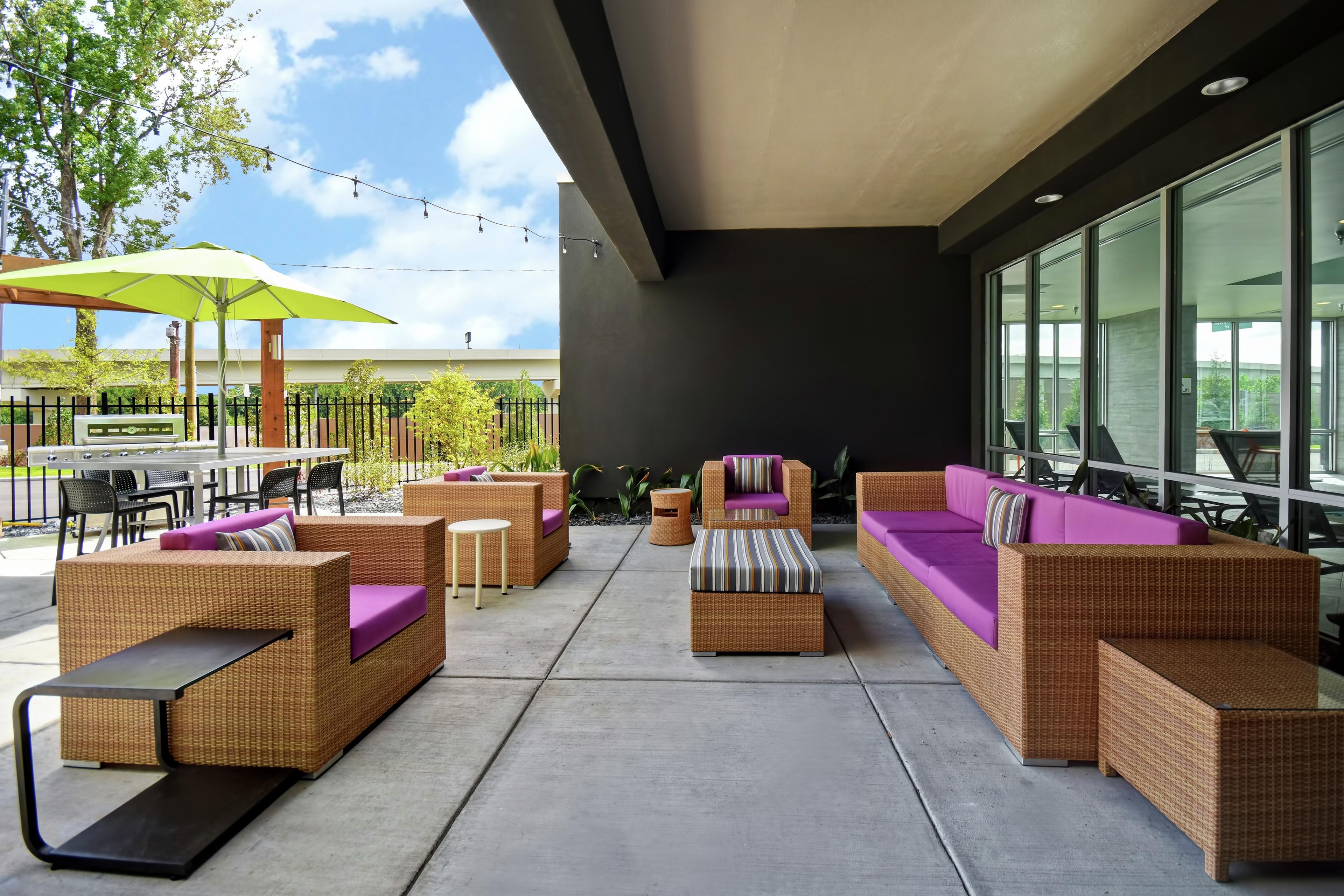 Área de estar externa com móveis de vime e uma mesa sob um guarda-sol verde.