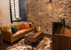 Uma sala de estar aconchegante com parede de pedra, um sofá de couro, uma mesa de centro de madeira e uma escrivaninha com abajur.