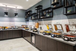 Disposição de buffet com diferentes estações de comida, incluindo uma estação de cachorros-quentes e um bar de saladas.