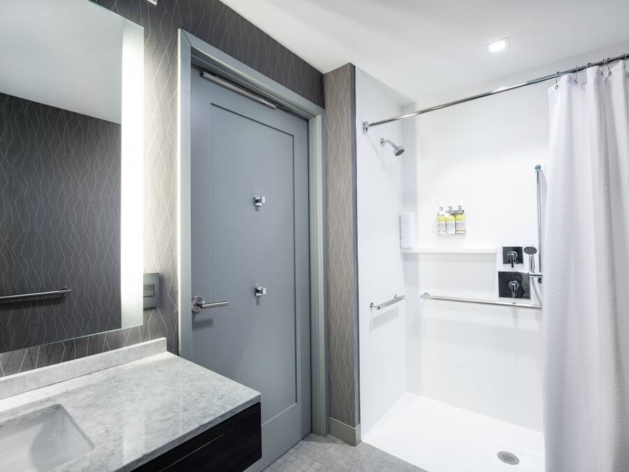 Casa de banho moderna com lavatório de mármore, cabine de duche em vidro e porta com toalheiro.