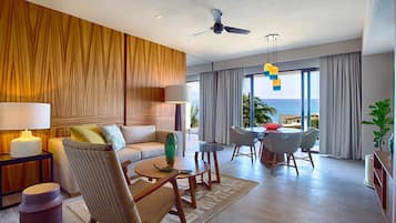 Quarto de hotel moderno com uma parede de destaque em madeira, um sofá, uma mesa de jantar com cadeiras, um ventilador de teto e vista para o oceano.