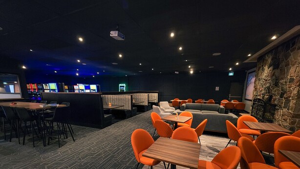 Uma área de estar moderna com poltronas laranja, um painel de pedra decorativo e um espaço de bar com máquinas de jogos.