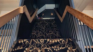 Uma escadaria com carpete estampado, um lustre moderno e corrimãos de madeira.