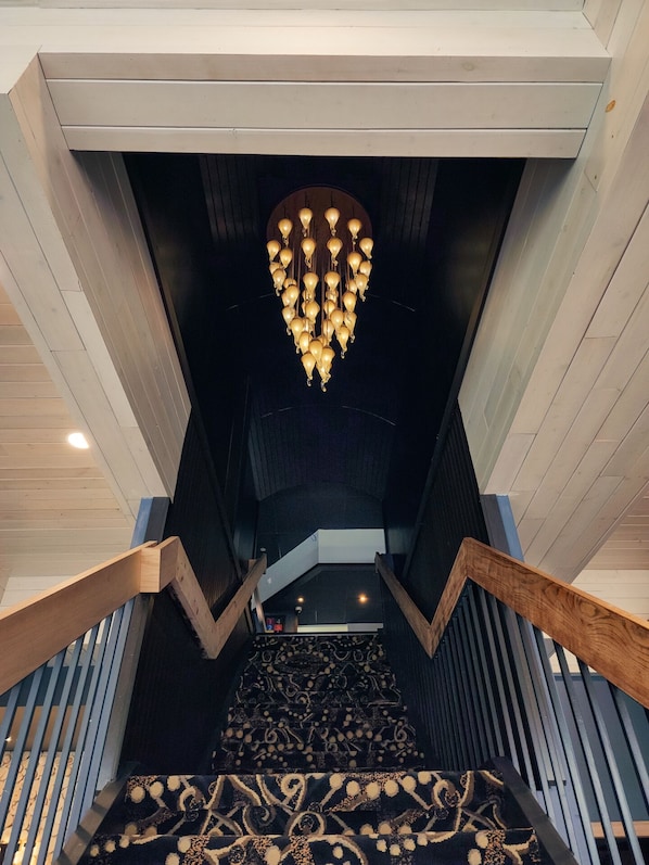 Uma escadaria com carpete estampado, um lustre moderno e corrimãos de madeira.