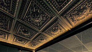 Uma área de refeições moderna com pé direito alto, detalhes em metal requintados, grandes janelas com vista para o exterior e uma mesa comprida com cadeiras.