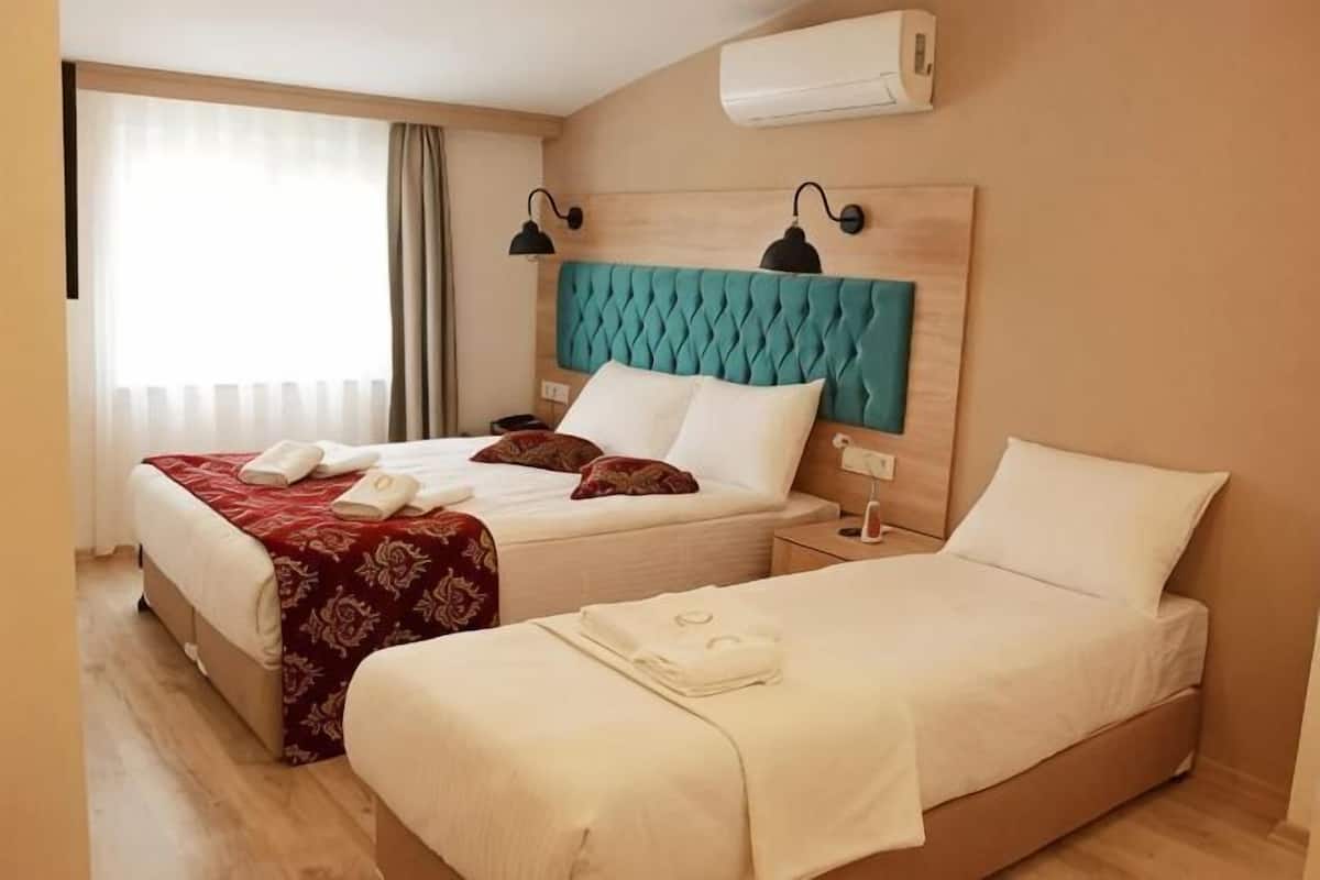 Quarto de hotel com duas camas, cabeceira de madeira, janela com cortinas e ar condicionado.