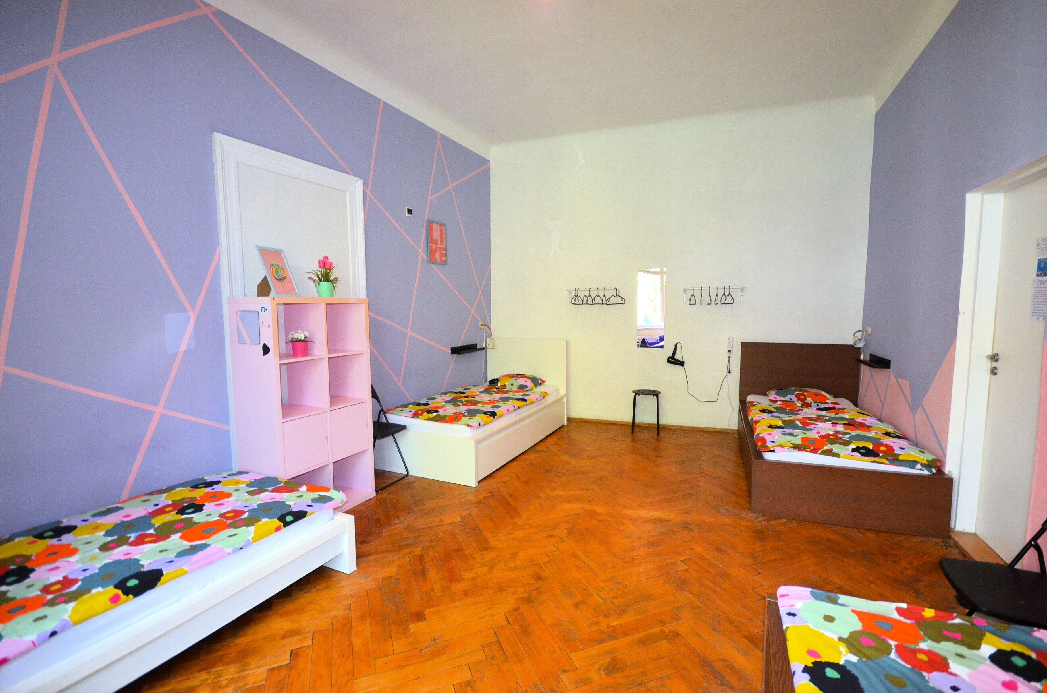 Quarto com duas camas, uma estante rosa e uma mesa pequena.
