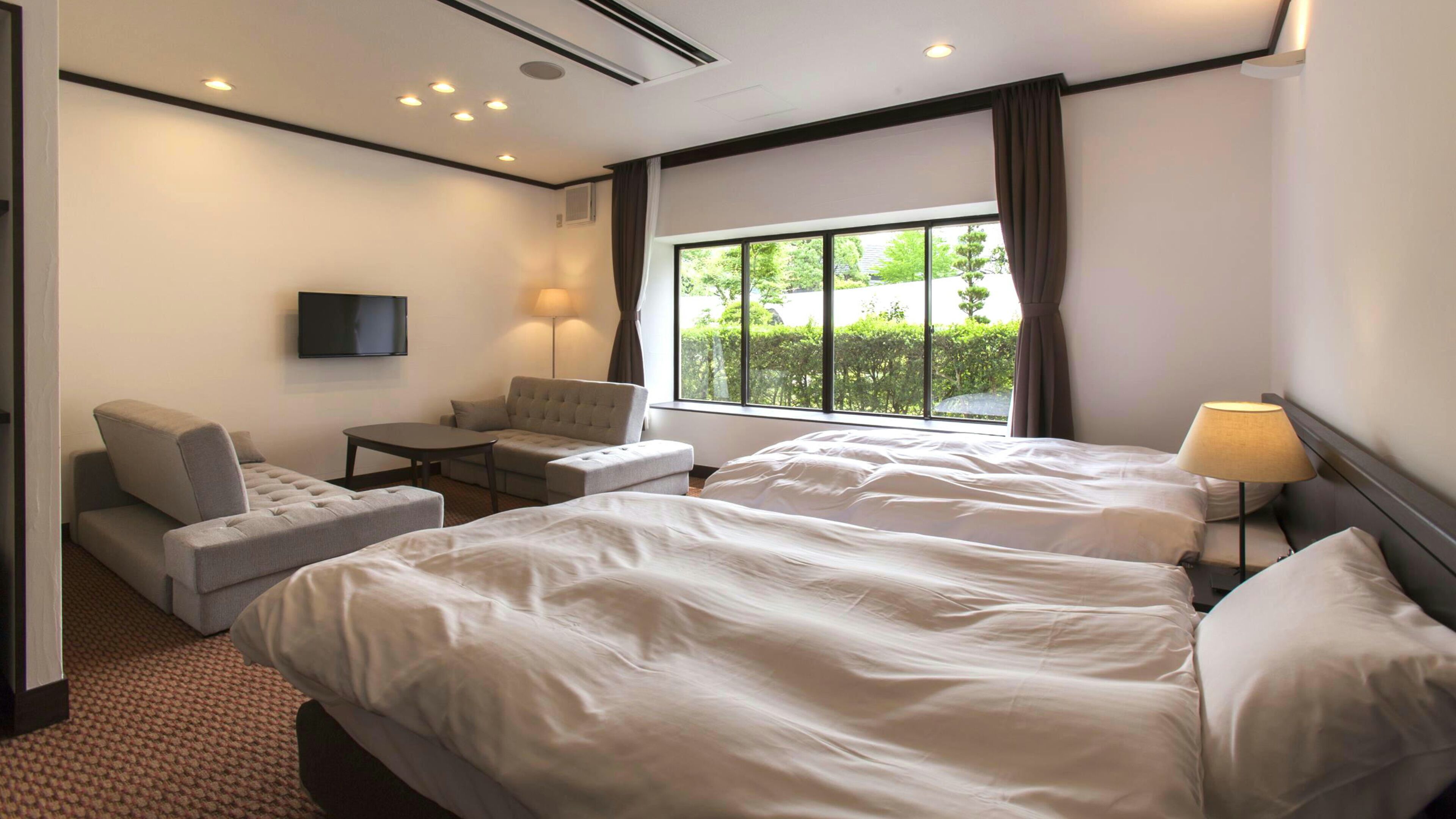 Quarto de hotel com duas camas, um sofá, uma mesinha, uma televisão e uma janela com cortinas.