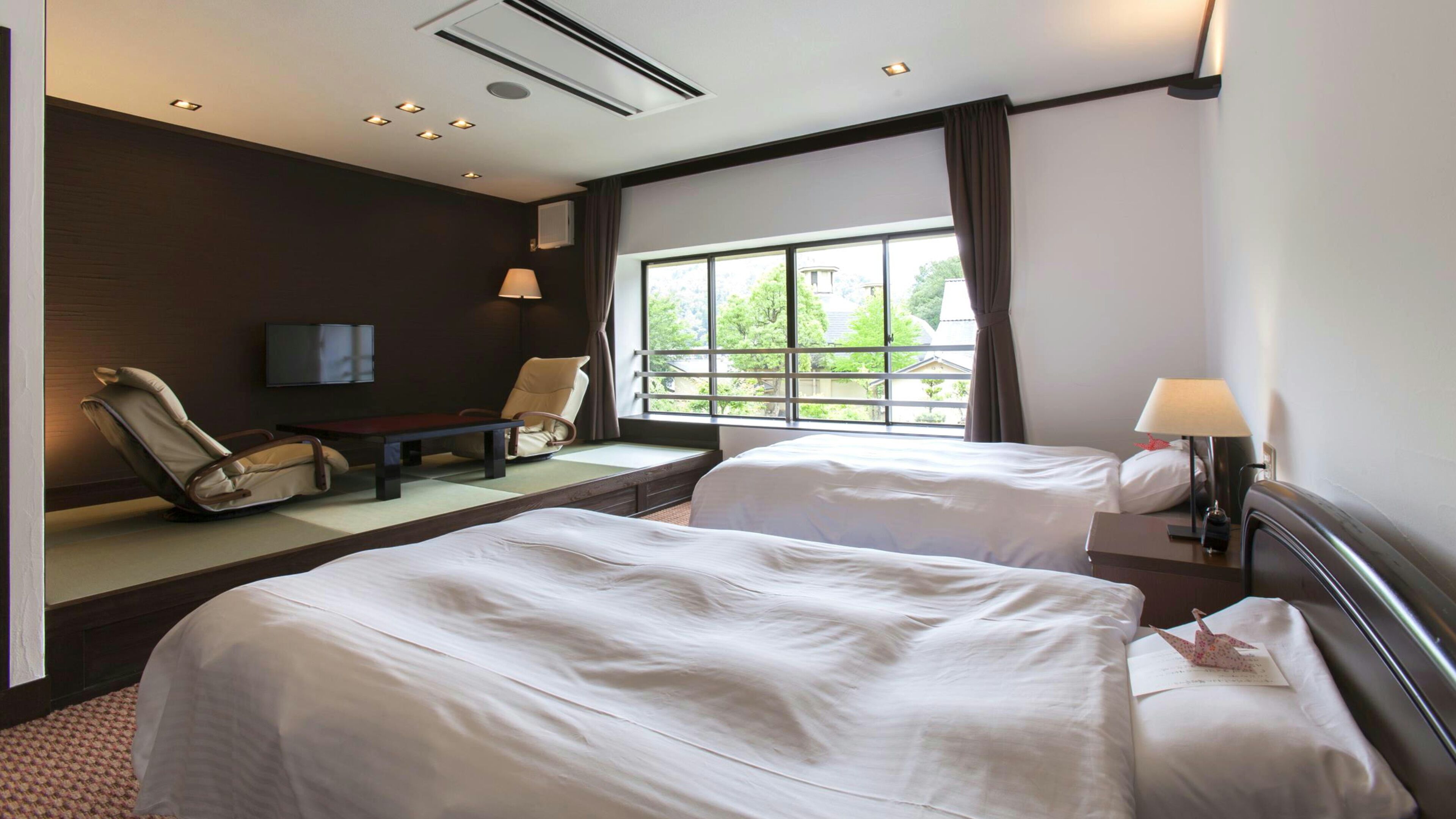 Quarto de hotel com duas camas, um sofá, uma televisão e uma janela com vista.