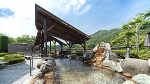 Uma onsen japonesa tradicional com um pavilhão de madeira, um caminho de pedra e paisagem natural.