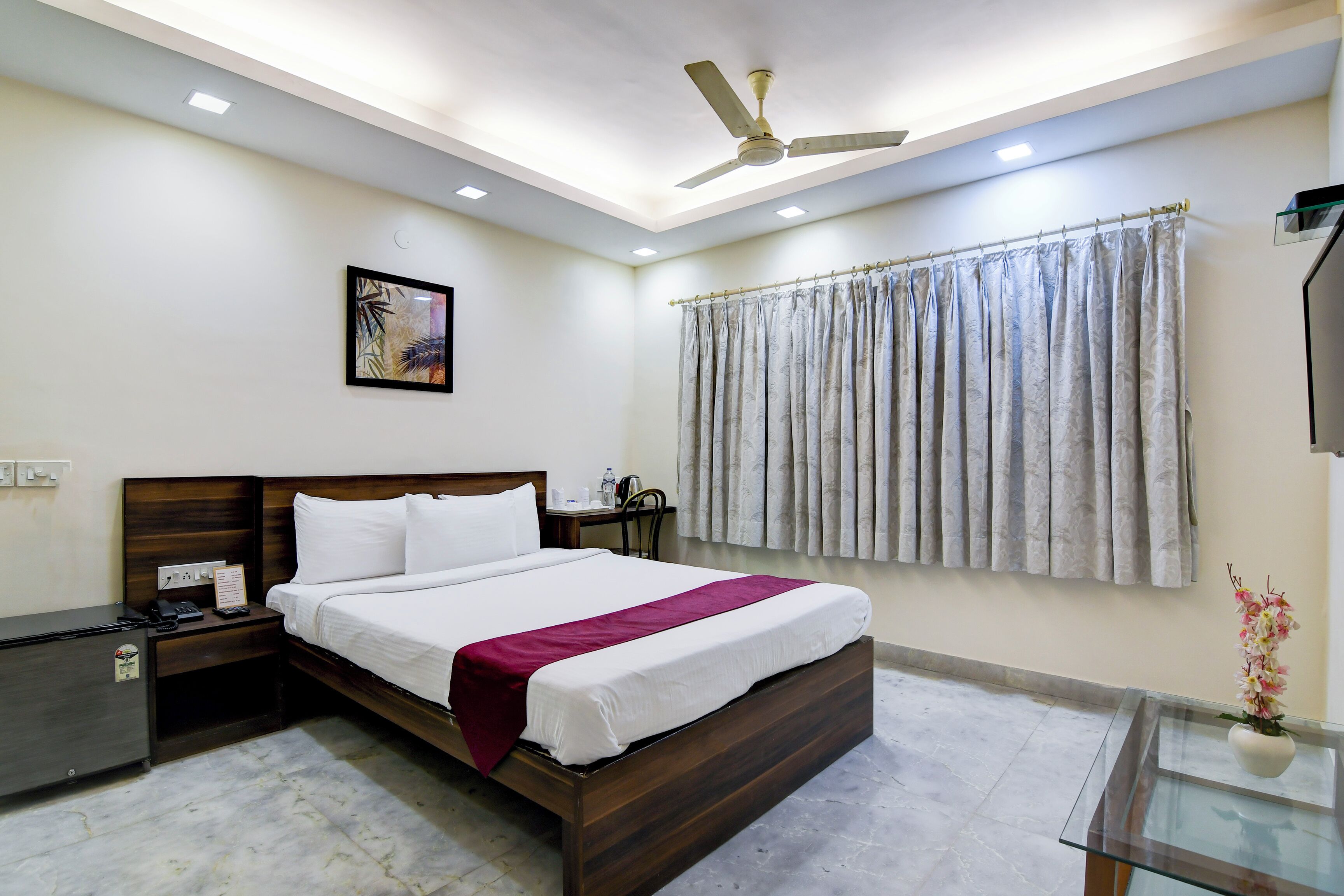Quarto de hotel com cama, mesa de cabeceira e ventilador de teto.