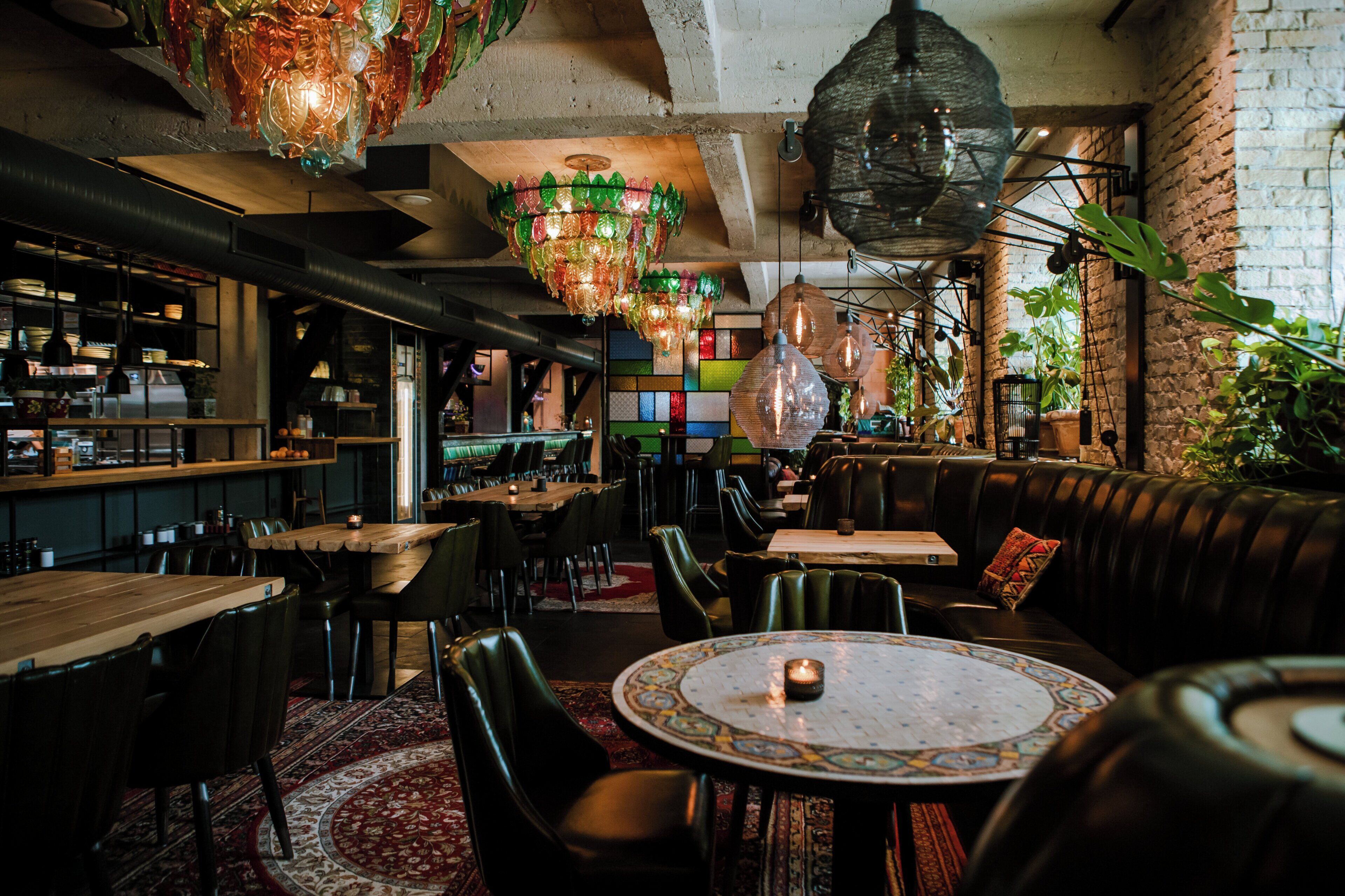 Interior acolhedor de restaurante com mesas de madeira, assentos de couro, luminárias pendentes e parede de tijolos.
