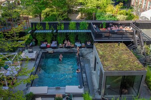 Uma área de piscina no terraço com estrutura de vidro, assentos de lounge e um deck coberto com vegetação.
