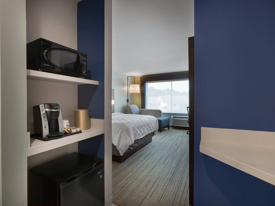 Quarto de hotel com cama, micro-ondas, cafeteira e luminária de mesa.