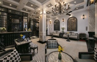 Um hall luxuoso com piso xadrez, mobiliário elegante, um balcão de recepção e um candelabro.