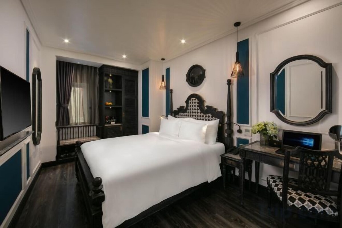 Quarto de hotel com uma cama grande, uma escrivaninha com cadeira, uma TV e um espelho.