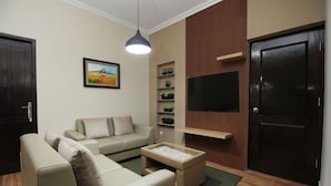 Sala de estar com um sofá bege, uma mesa de centro, televisão fixada na parede e uma porta.