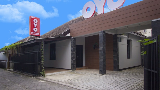 Um edifício com um grande letreiro 'OYO', uma entrada coberta e um caminho pavimentado.