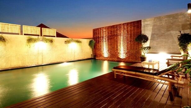 Um deck de madeira com piscina, cadeiras de descanso e um muro com ripas verticais.