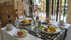 Uma mesa de jantar posta com pratos de comida, um vaso com planta e um copo de água.