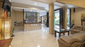 Um hall de hotel com uma mesa de recepção, um sofá, uma mesa de centro e uma TV fixada na parede.