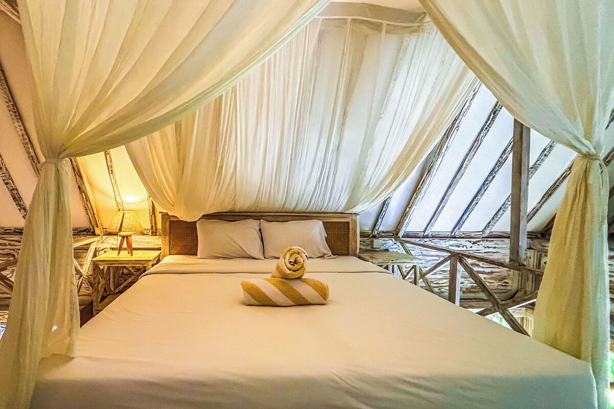Quarto com cama, mesa de cabeceira, luminária e janela com vista do céu.