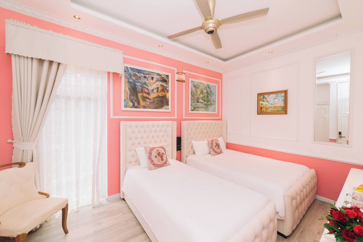 Quarto de hotel com duas camas, um ventilador de teto e obras de arte nas paredes.