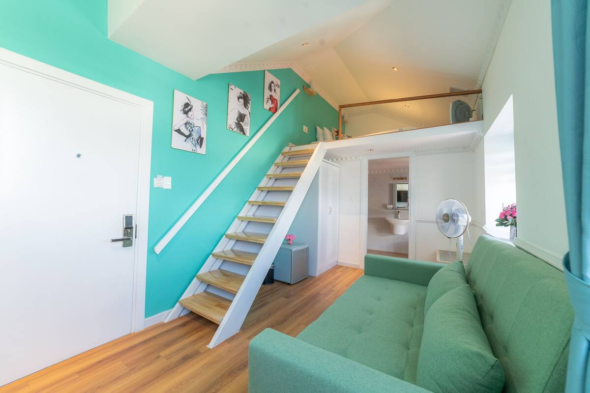 Uma sala de estar com parede verde-água, escada de madeira, sofá verde e porta branca.