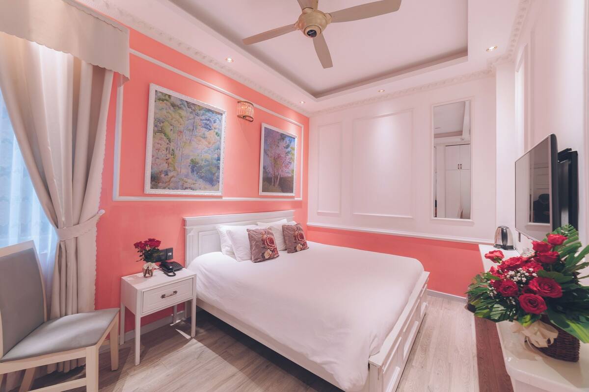 Quarto com cama, mesa de cabeceira, cadeira e ventoinha no teto.