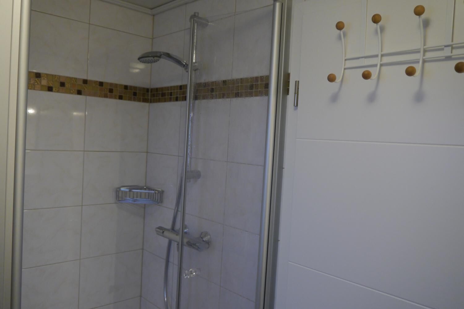 Um chuveiro com divisória de vidro, um chuveiro manual e uma torneira fixada na parede.