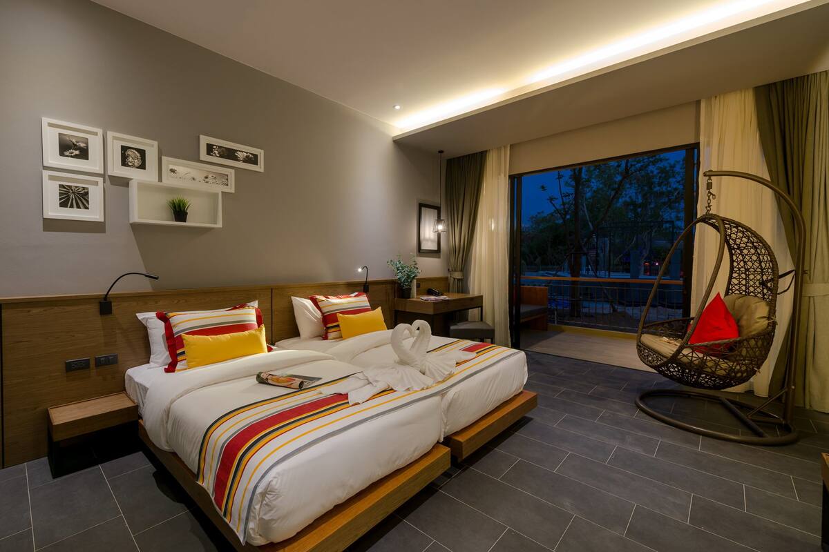 Quarto de hotel moderno com uma cama grande, uma cadeira suspensa e vista para o exterior.