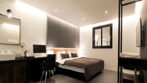 Quarto de hotel moderno com cama, escrivaninha e cadeira, um espelho grande e uma televisão.