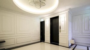 Um corredor amplo com piso lustroso, painéis brancos e um lustre moderno.