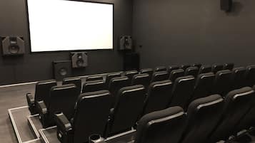 Um cinema com fileiras de assentos pretos, uma tela grande e alto-falantes nas paredes.