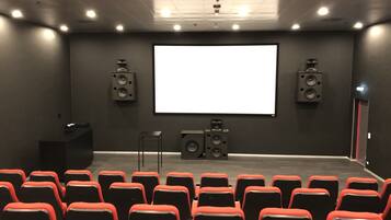 Um teatro com fileiras de assentos vermelhos e pretos, uma tela grande e alto-falantes em ambos os lados.