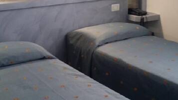 Quarto com duas camas, parede com padrão de tijolos, uma mesinha com telefone e uma luminária fixada na parede.
