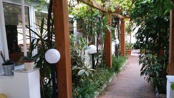 Caminho coberto no jardim, com vigas de madeira e plantas em vasos.