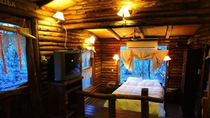 Um quarto de cabana de madeira aconchegante, com uma cama, televisão e janela com cortinas.