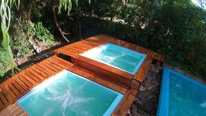 Um deck de madeira com duas banheiras de hidromassagem, cercado por vegetação.