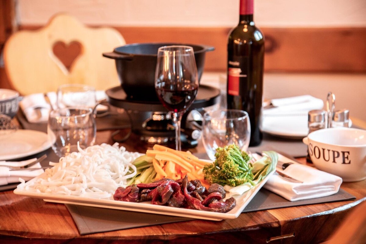 Uma mesa de jantar com um prato de comida, uma garrafa de vinho e uma tigela com a etiqueta 'SOUPE'.