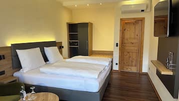 Quarto de hotel moderno com uma cama grande, um guarda-roupa de madeira, uma televisão e uma pequena mesa com copos.