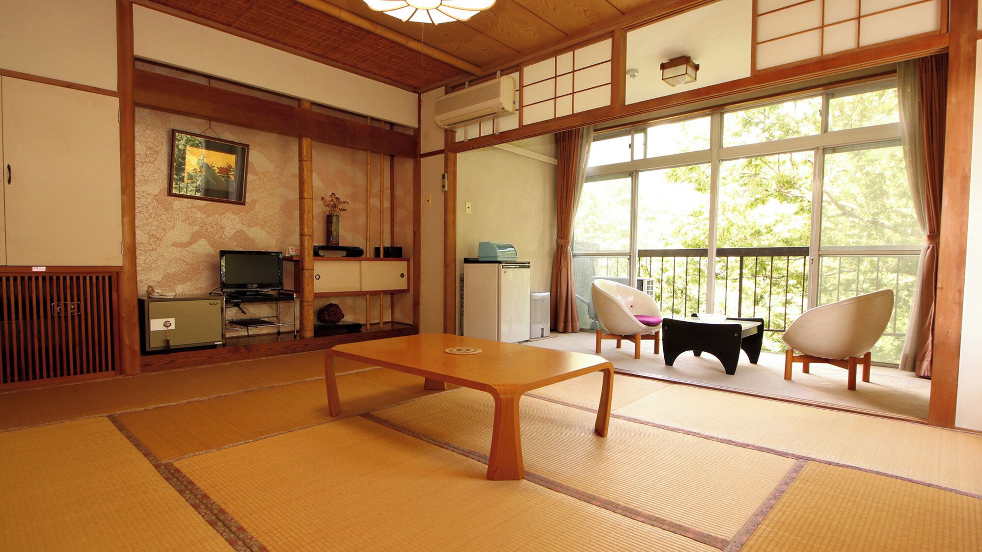 Quarto japonês tradicional com tatames, televisão, pequeno frigorífico e vista para o verde através de amplas janelas.