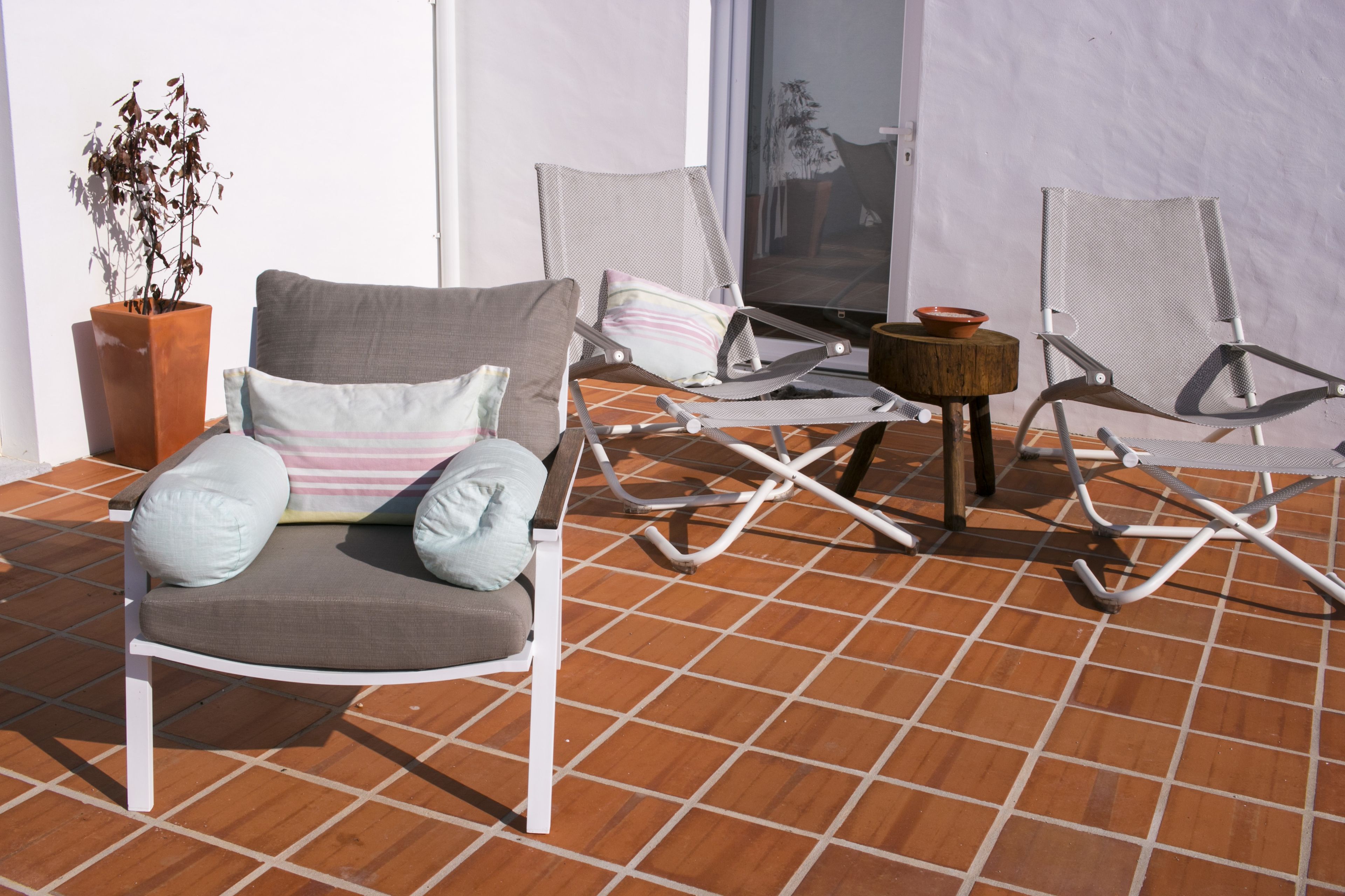 Um terraço com uma cadeira branca, uma cadeira estofada e uma pequena mesa com uma tigela.