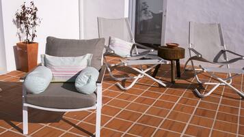 Um terraço com uma cadeira branca, uma cadeira estofada e uma pequena mesa com uma tigela.