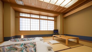 Quarto japonês tradicional com tatames, duas camas com roupa de cama colorida, uma mesa de madeira e uma grande janela com vista.