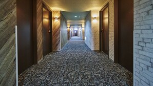 Corredor de hotel com paredes de madeira, carpete estampado e portas em ambos os lados.