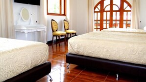 Quarto de hotel com duas camas, uma toucador com espelho, duas cadeiras e uma janela grande com vista.