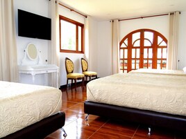 Quarto de hotel com duas camas, uma toucador com espelho, duas cadeiras e uma janela grande com vista.