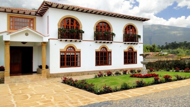 Uma casa de dois andares com fachada branca, telhado de telhas vermelhas e várias janelas com sacadas.